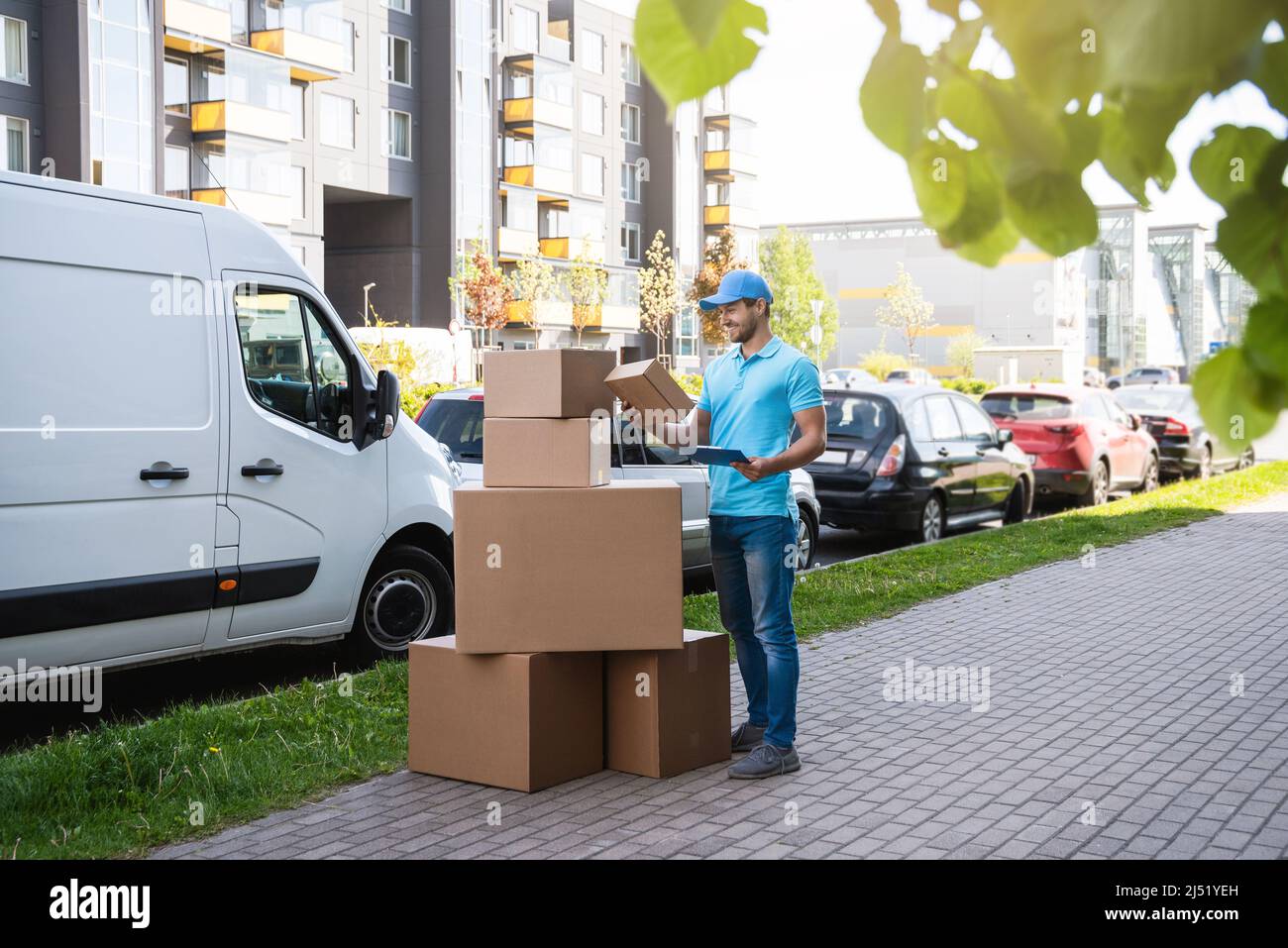 Happy delivery man with a lot of cardboard boxes near his van on a city ...