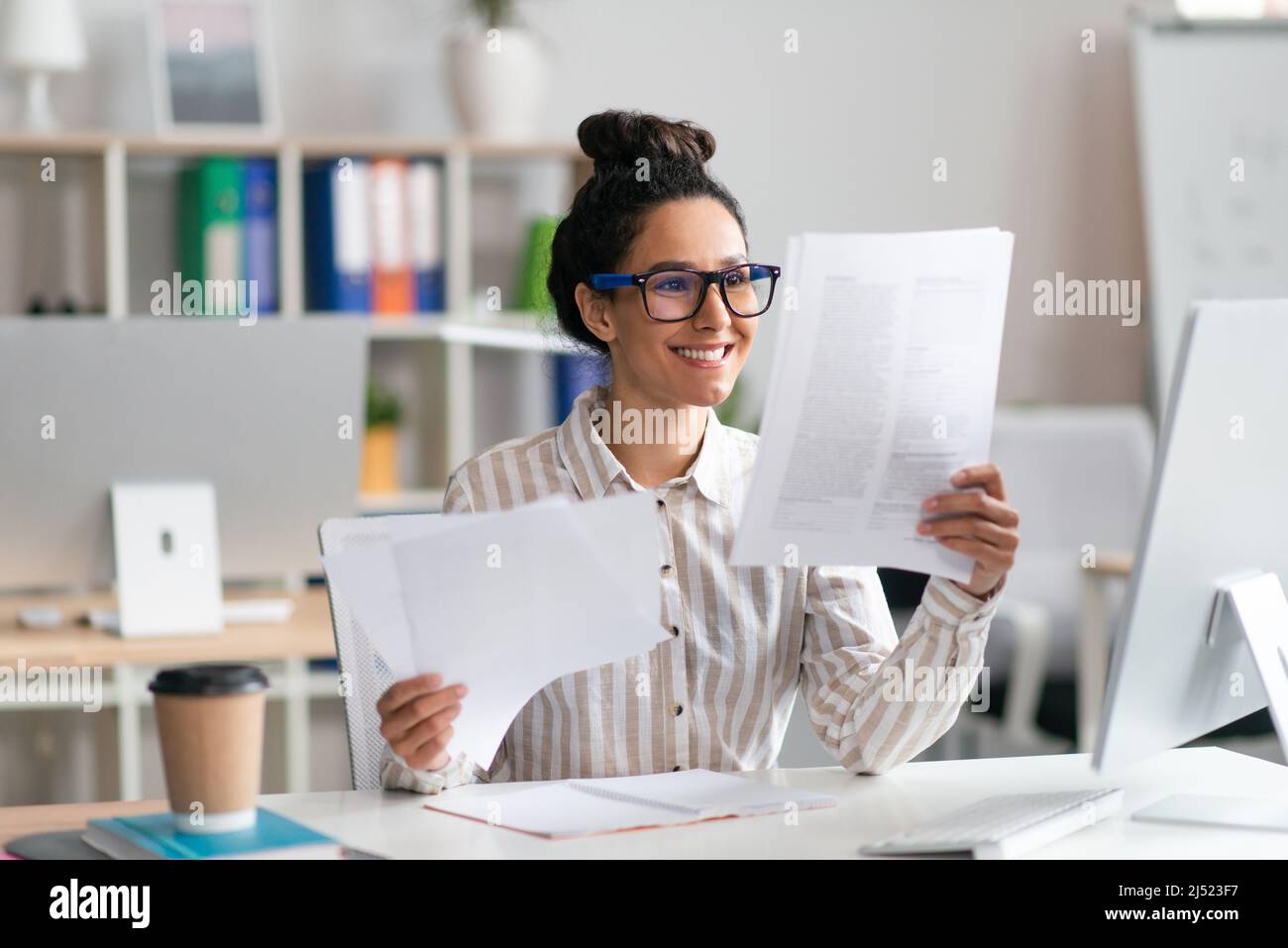 Happy latin businesswoman looking through documents at her desk in ...