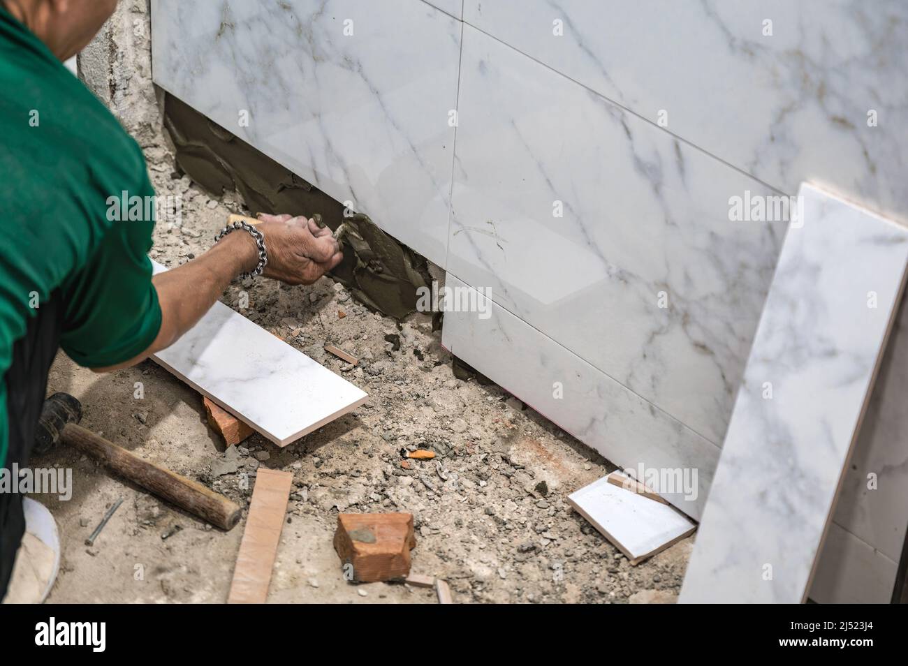 Male tiler using trowel laying marble tile with cement in bathroom ...
