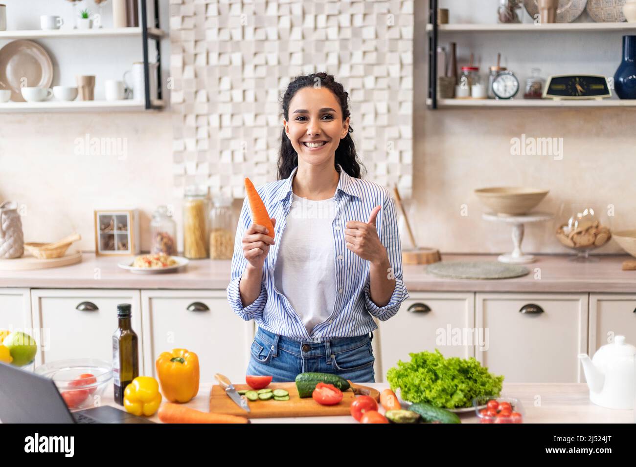 Happy latin woman holding carrot and gesturing thumb up, approving ...