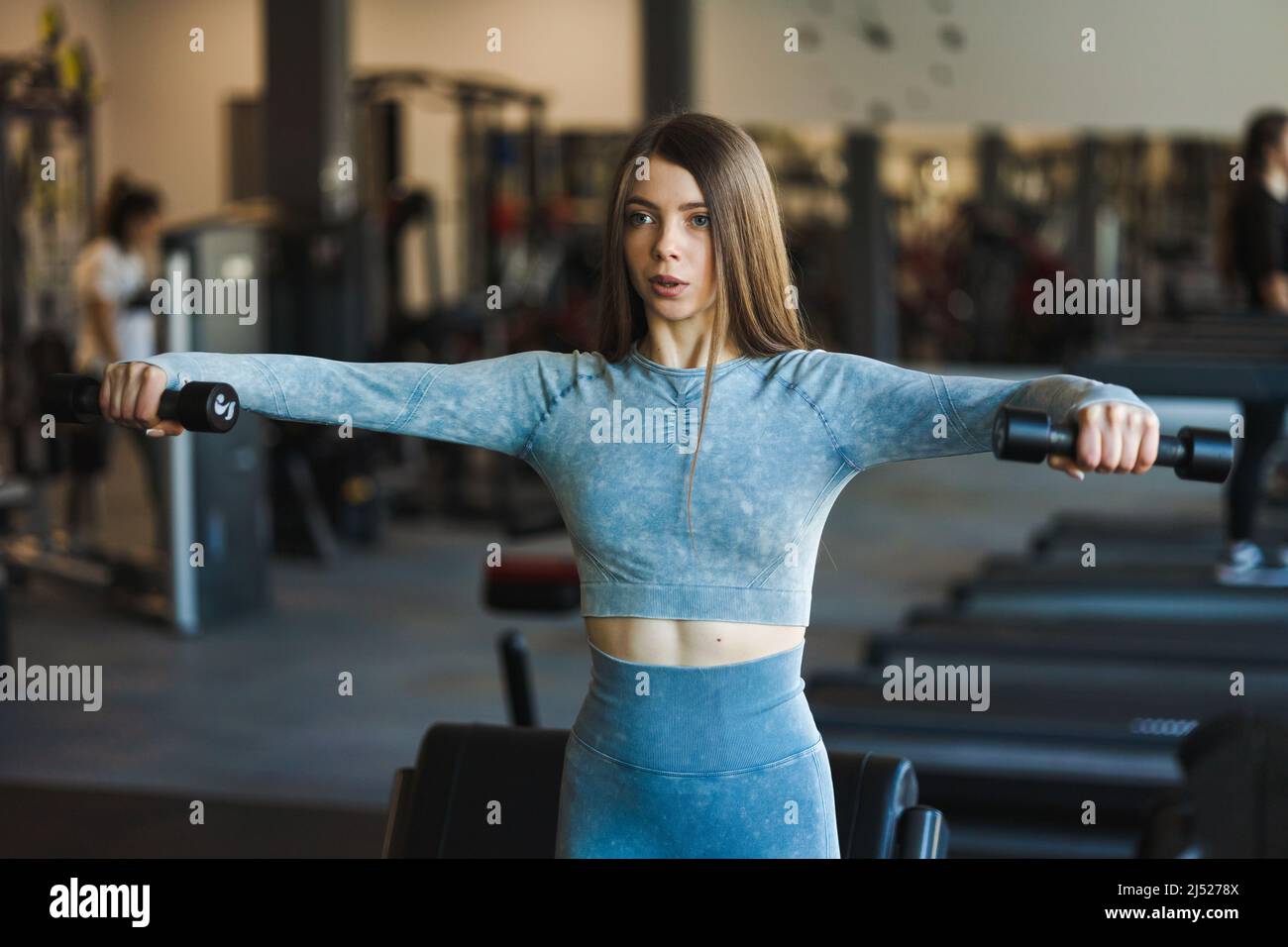 Slender fitness girl in blue sportswear does exercises with dumbbells ...