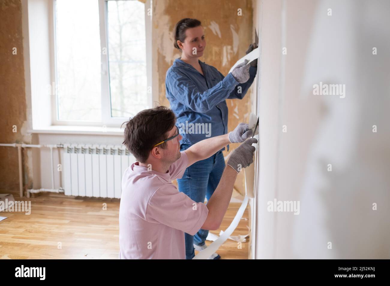 Young caucasian couple removing old wallpaper from walls preparing for ...