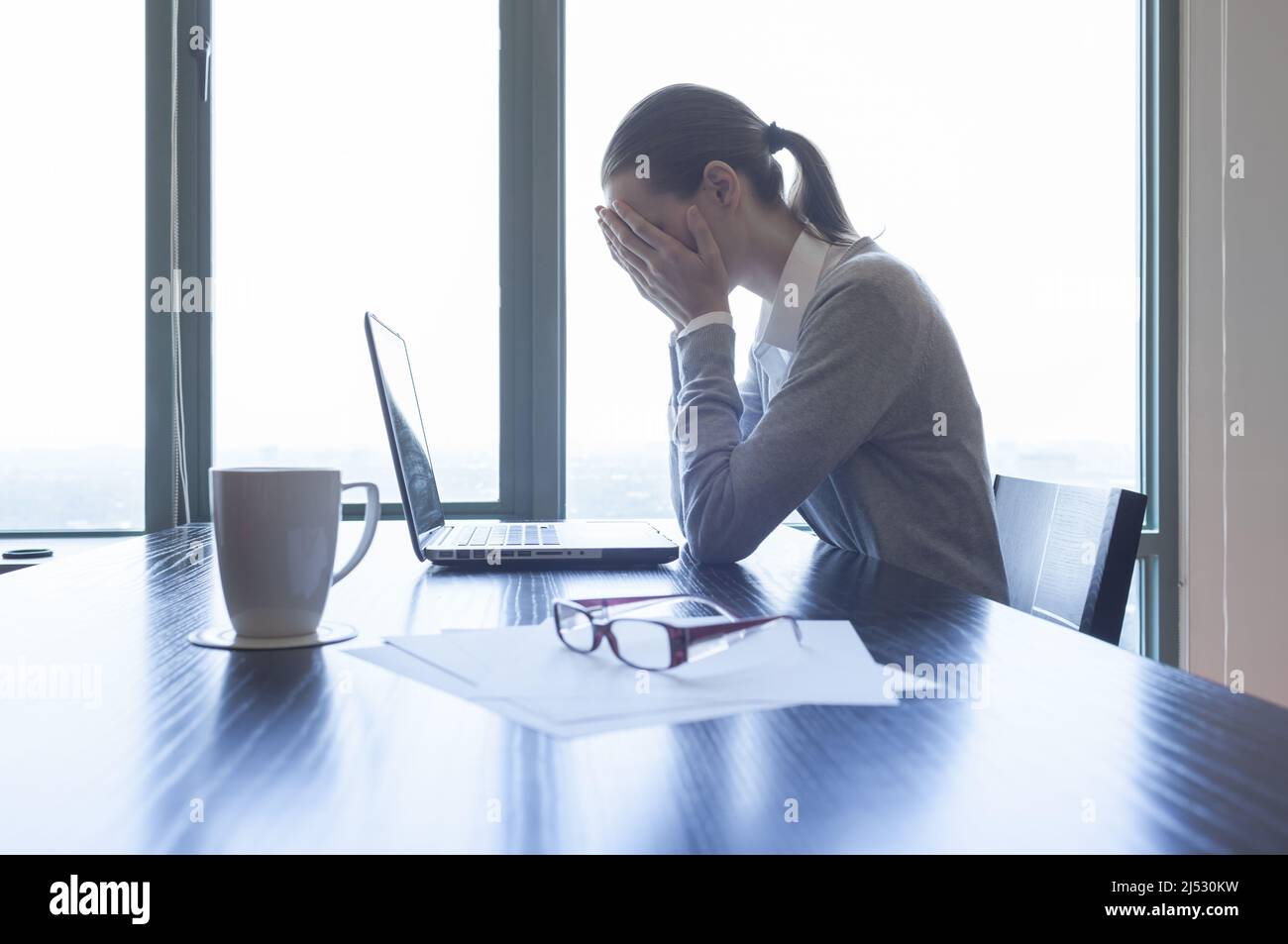 Stressed businesswoman at office computer with hand over her face ...