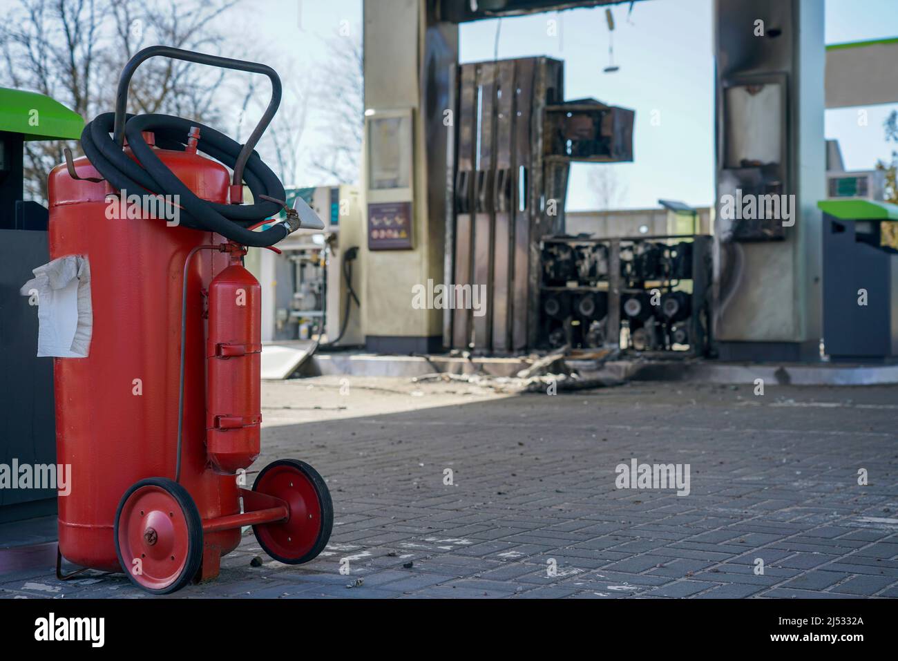 Red fire extinguisher in the parking lot after the fire. Gas station ...