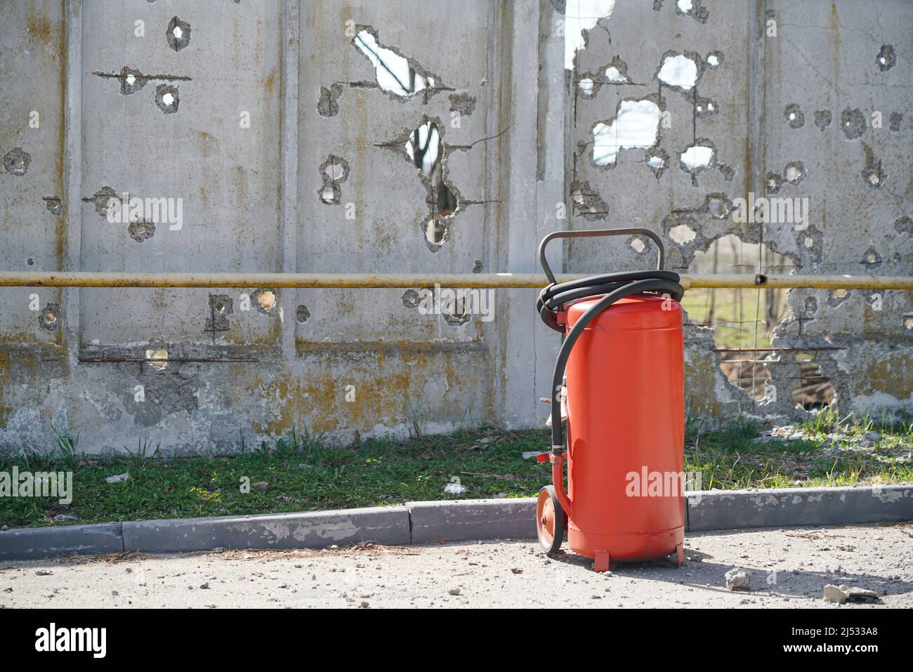 A red balloon fire extinguisher stands near a shelled concrete fence ...