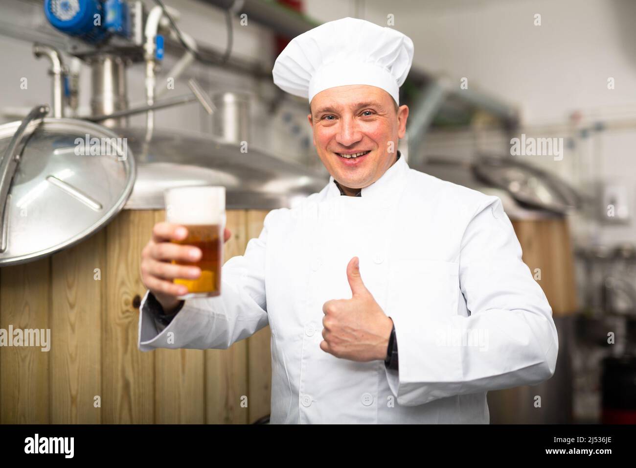 Brewer is standing with beer with foam in glass on his workplace Stock ...
