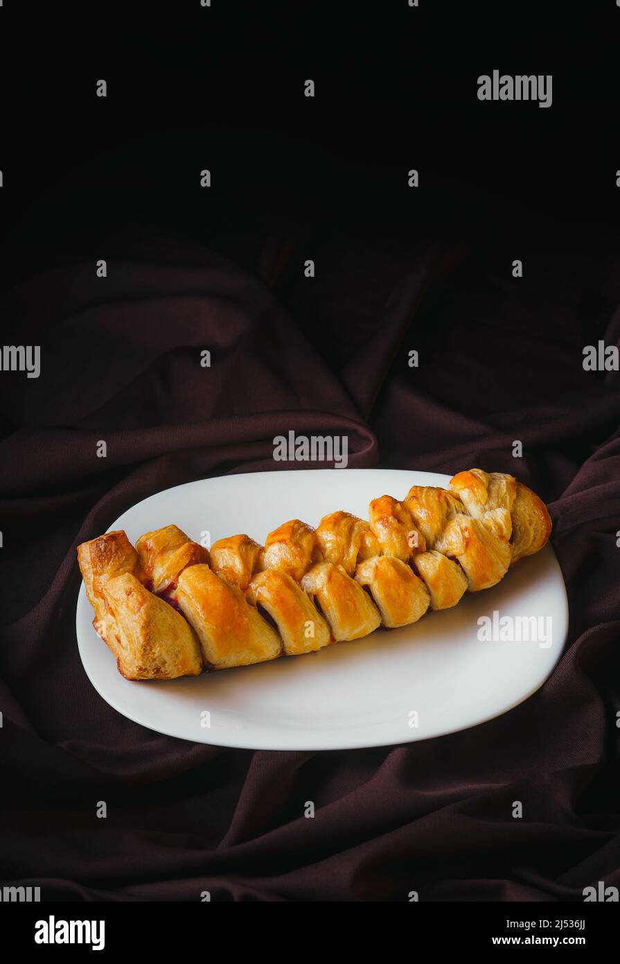 Homemade braided bread filled with strawberry jam on a white plate with ...