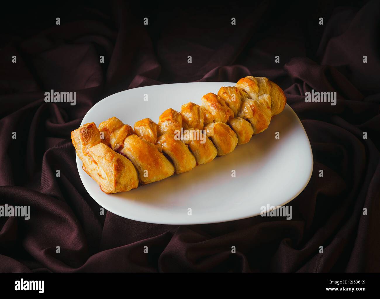 Homemade braided bread filled with strawberry jam on a white plate with ...