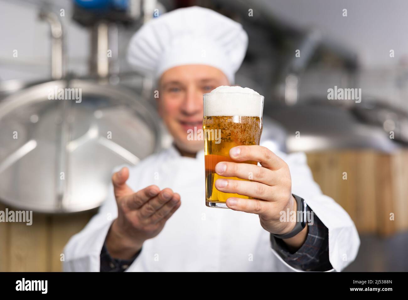 Brewer is standing with beer with foam in glass on his workplace Stock ...