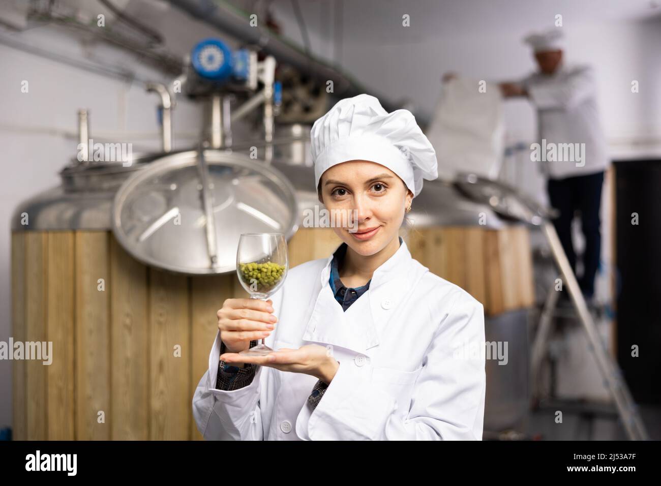 Portrait of a positive female brewer with a glass of hops at brewery ...