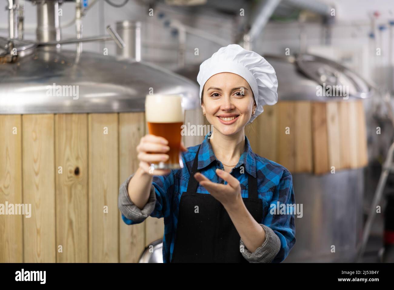 Portrait of female brewer who is standing with glass of beer on his ...