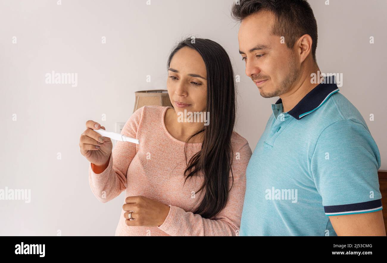 couple of man and woman expectantly looking at a pregnancy test at home ...