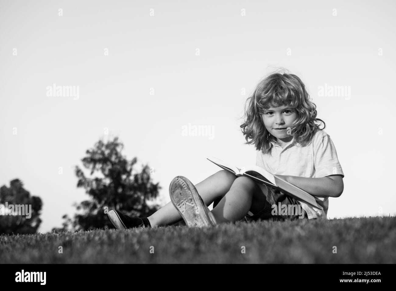 Clever child boy reading book laying on grass and sky background with ...