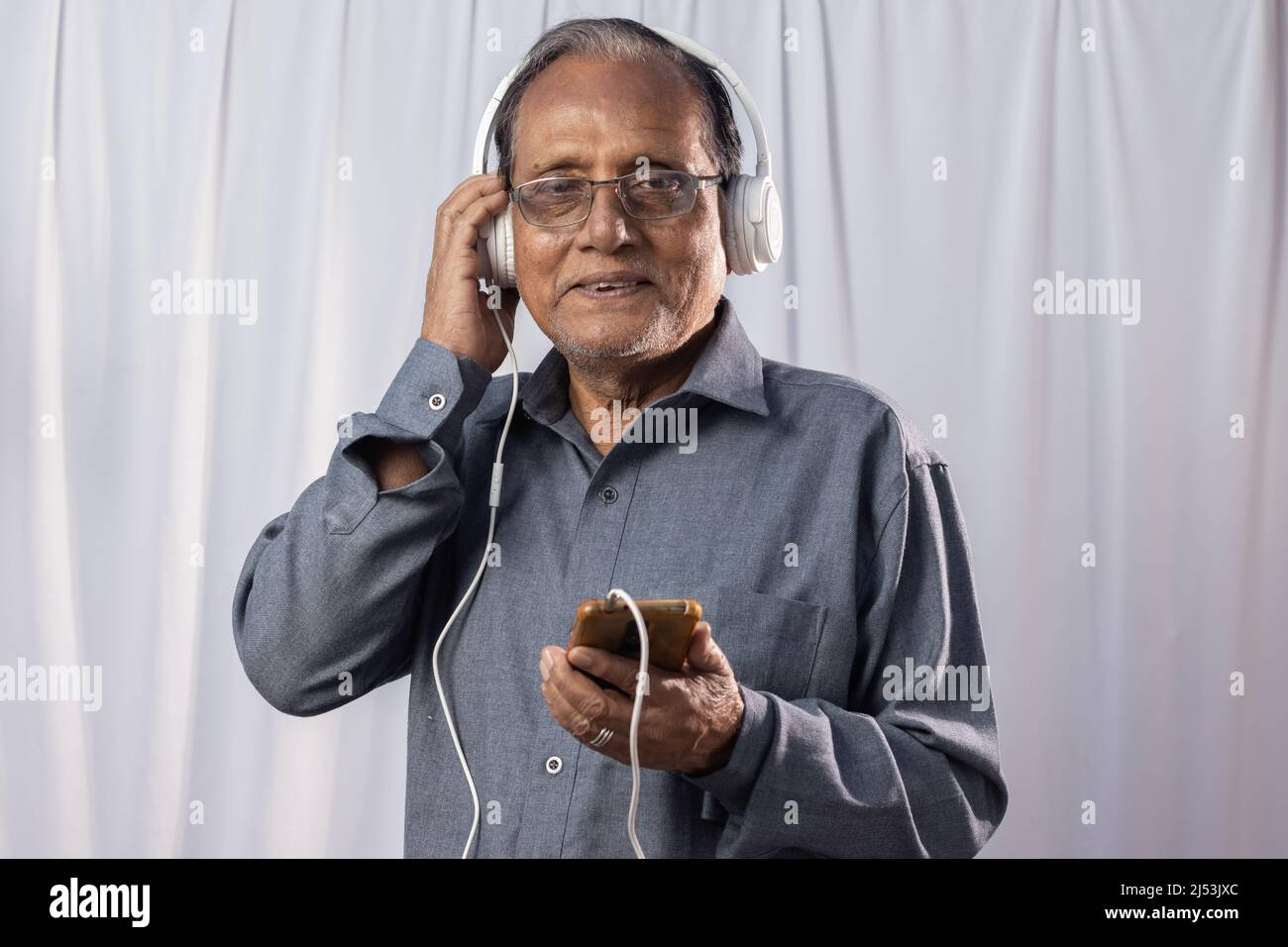 An Indian old person listening to music with smart phone and headphone ...