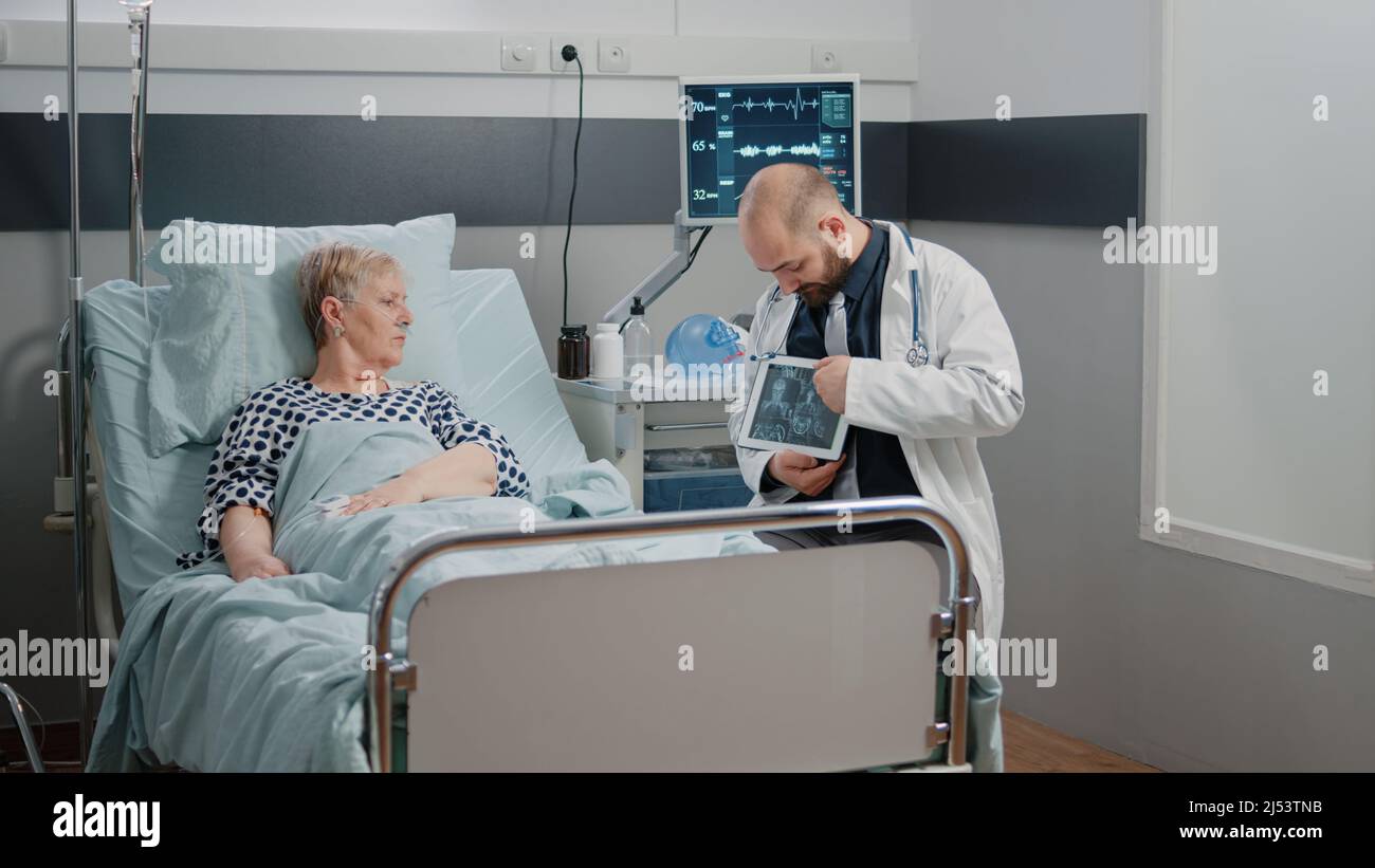 Medic pointing at tablet display with radiography for ill woman in bed ...