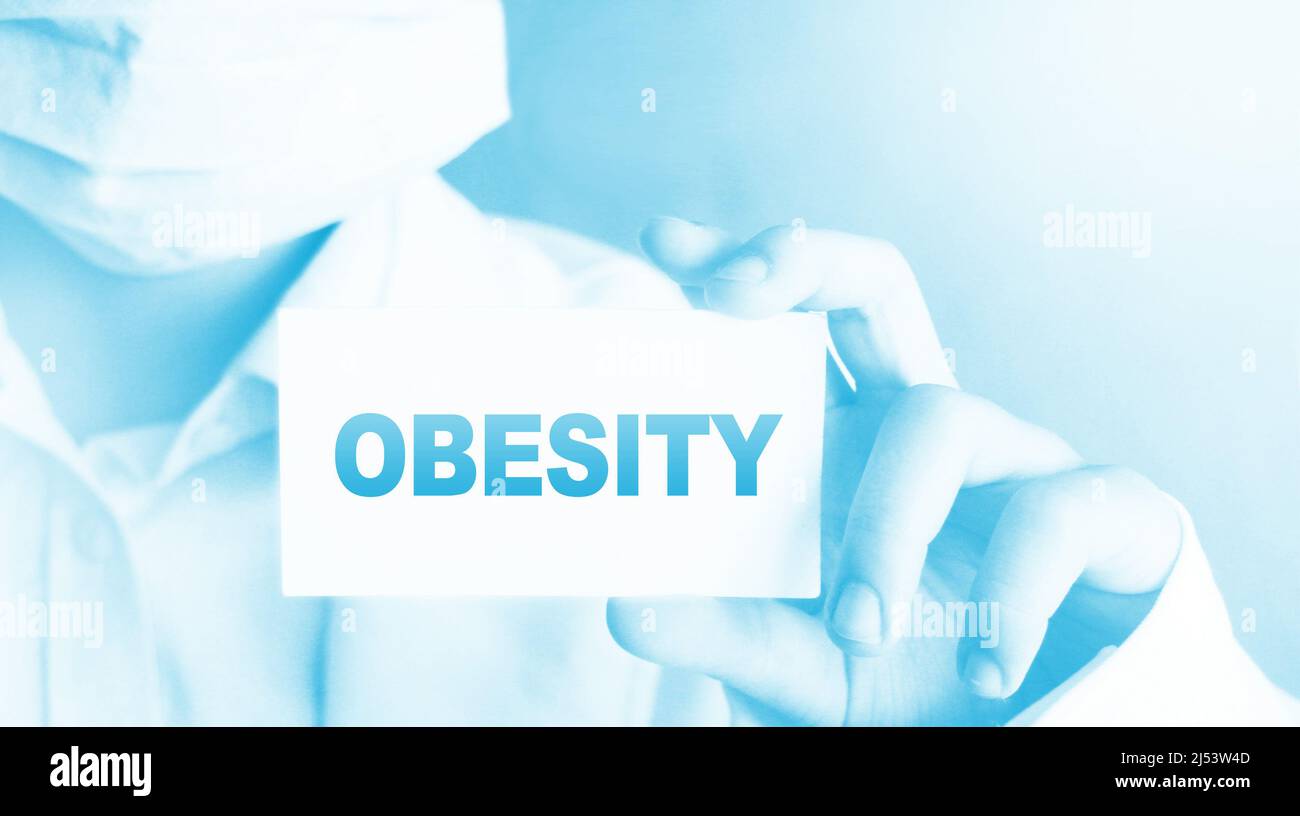 Obesity word on card shown by a Doctor with surgical mask on his face ...