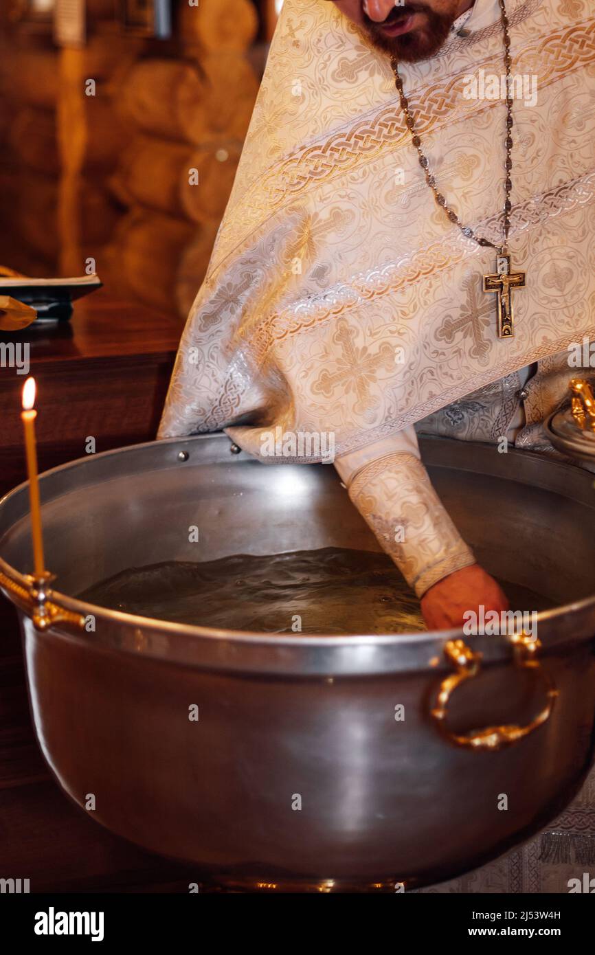 Unrecognizable bearded priest in silver cassock stand at metal font ...