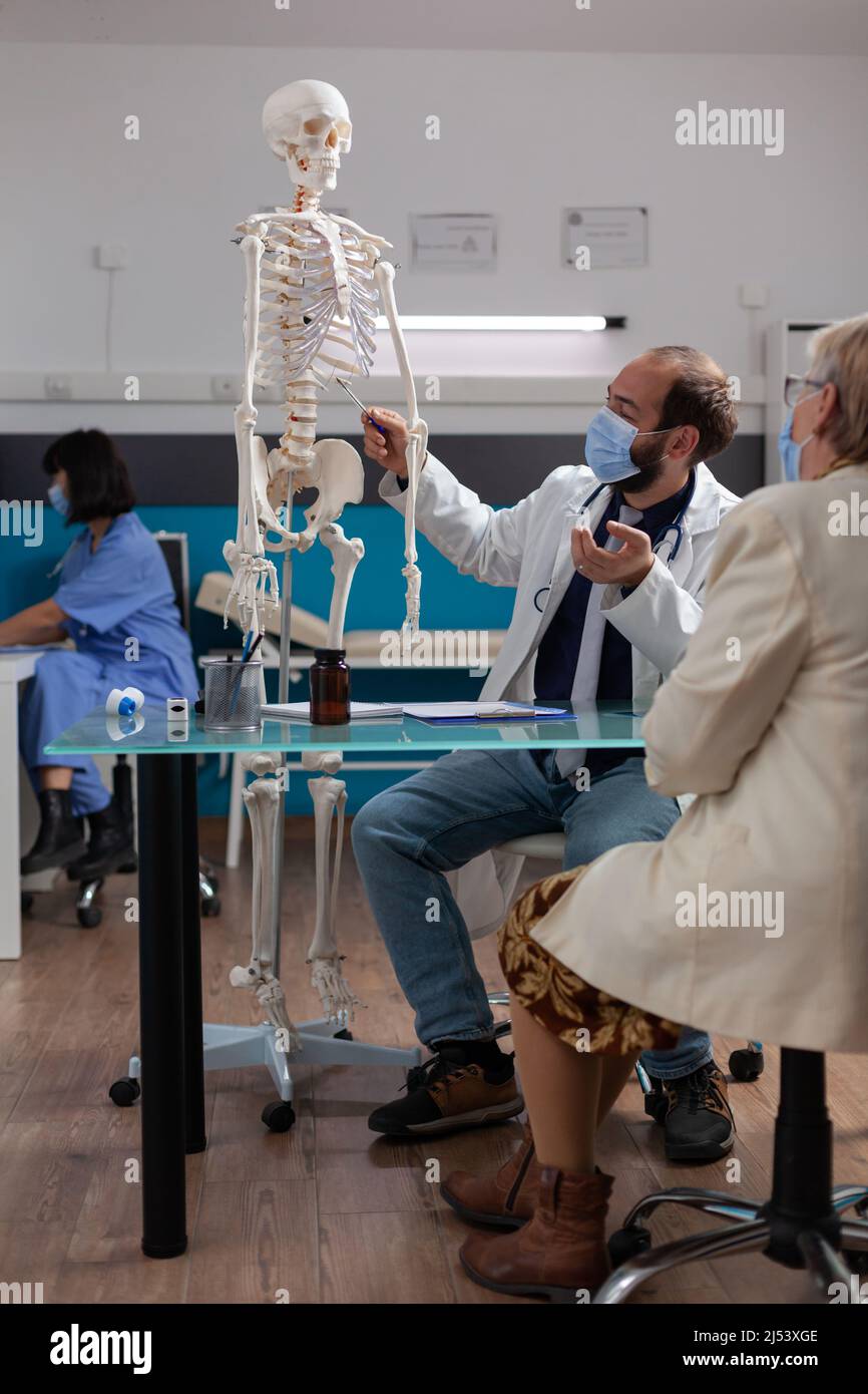 Physician showing human skeleton to pensioner woman at exam appointment ...