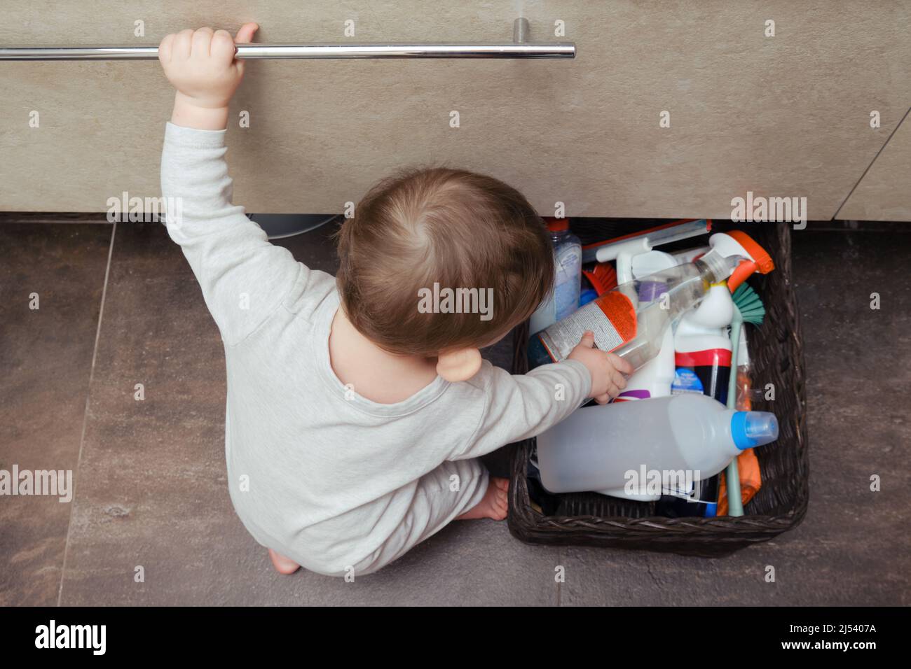 Toddler baby boy is playing in the toilet room with cleaning detergents ...