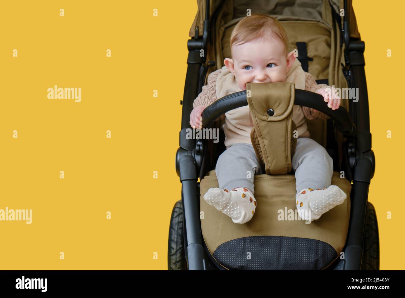 A happy child is sitting in a baby carriage on a studio yellow ...