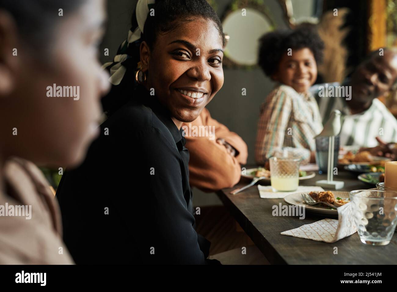 African happy woman talking to her family while sitting at dining table ...