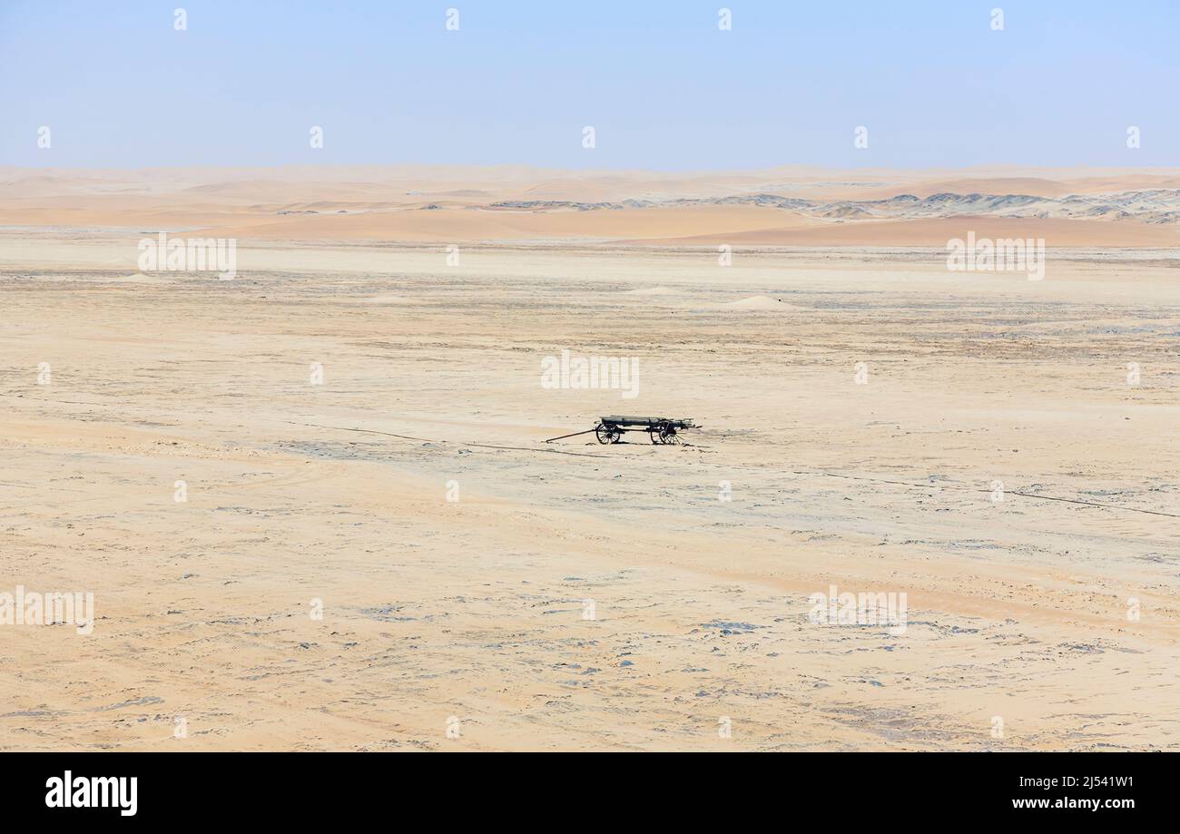 An abandoned, disintegrating wooden cart stands in the sand of the vast ...
