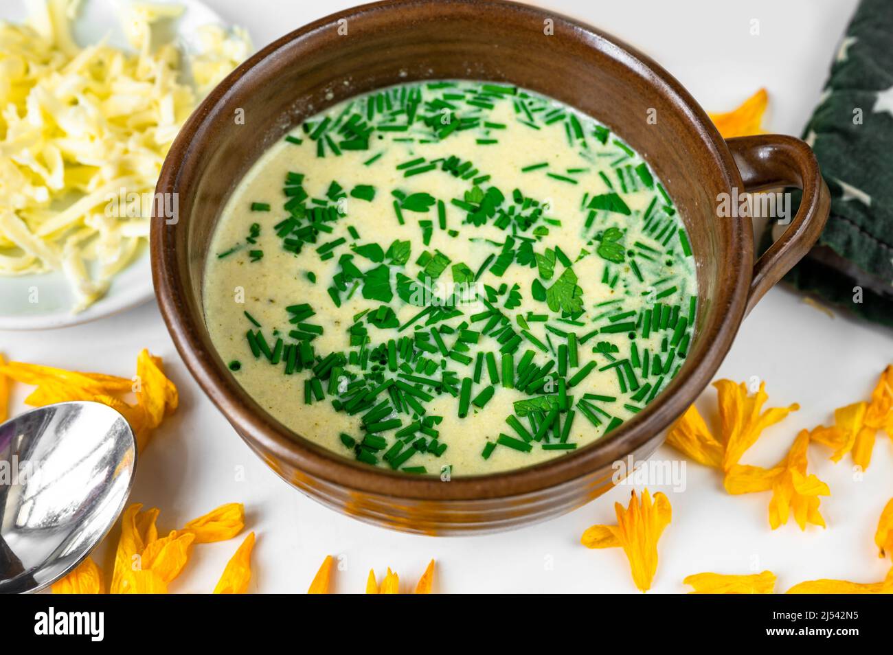 Creamy chive soup in brown bowl, grated butter, many yellow dried ...