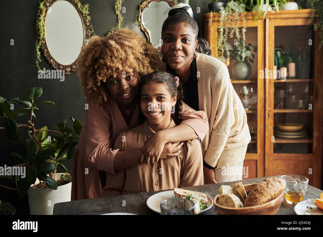 Portrait of three sisters embracing and smiling at camera while sitting ...