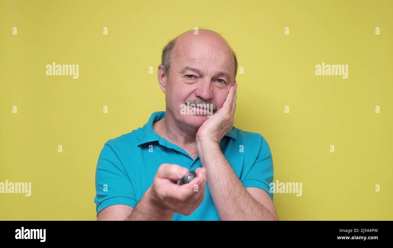Senior bored man switches the channels by pressing the buttons on the ...