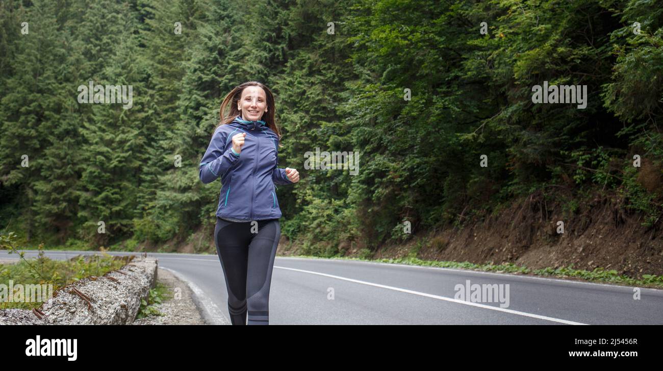 Young fitness woman running on the road through the forest Stock Photo ...