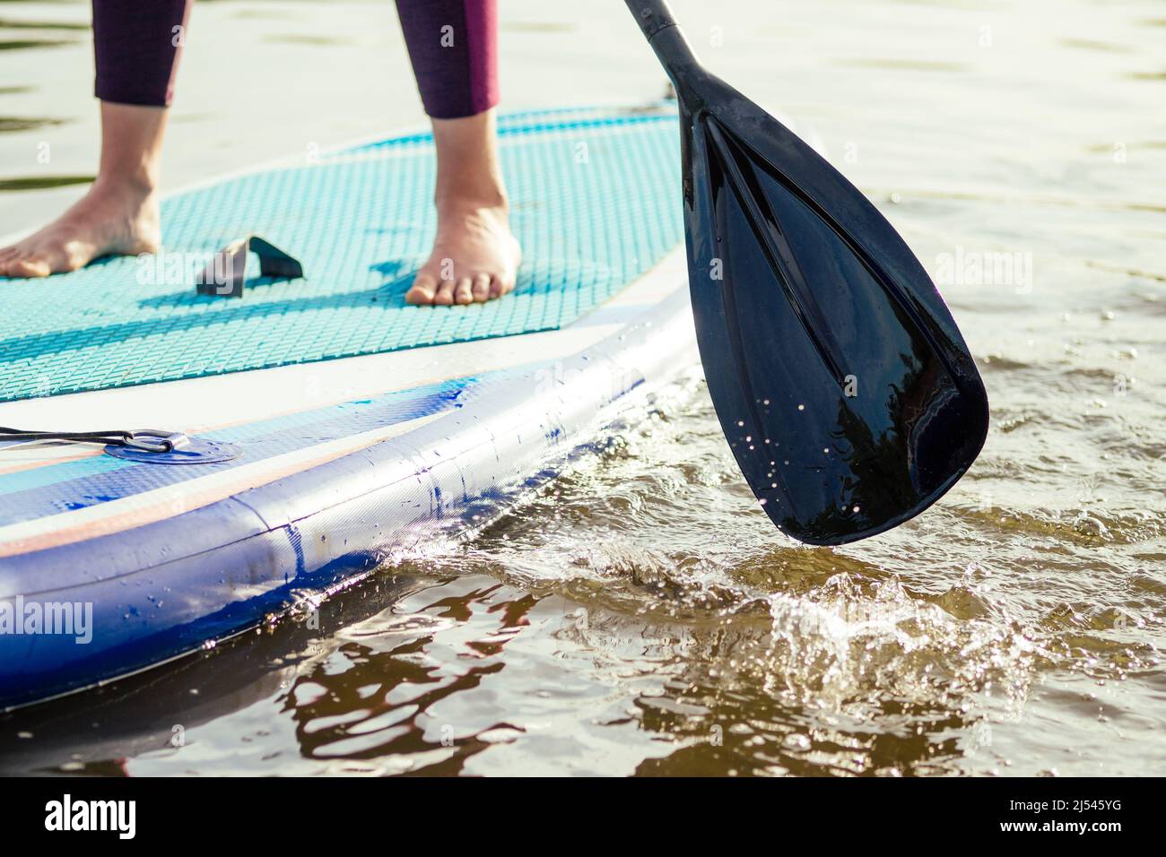 Stand up paddle boarding on a quiet sea lake , close-up of legs and ...