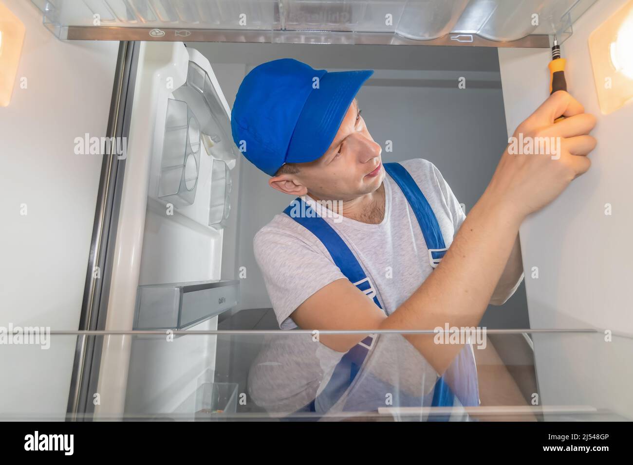 Male technician in overalls repairs a broken refrigerator with a ...