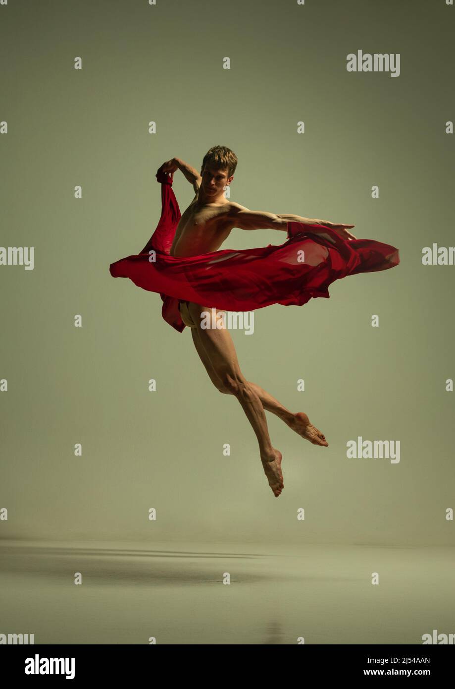 One young muscled man, flexible ballet dancer in action with red fabric ...