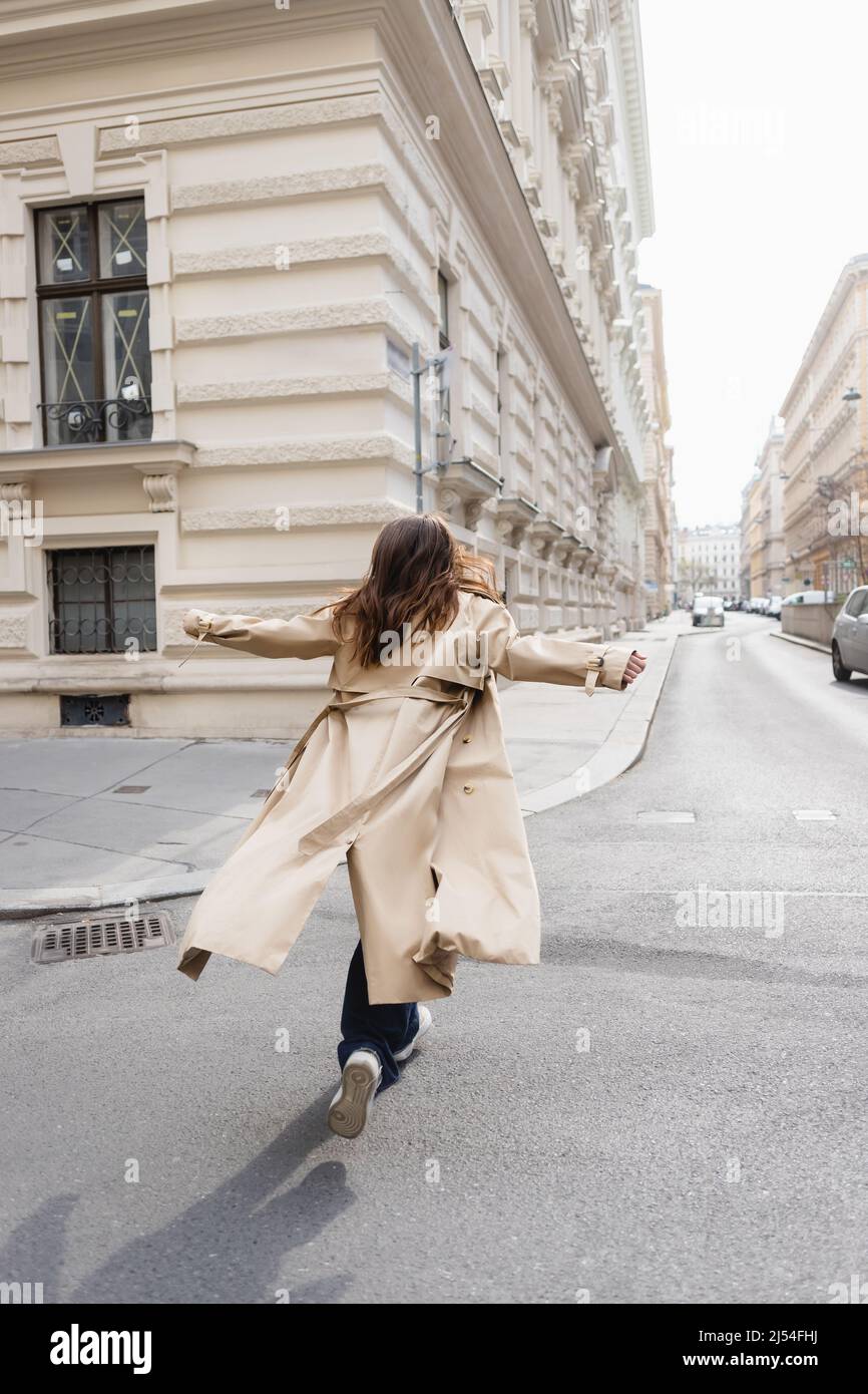 back view of woman in beige trench coat walking with outstretched hands ...