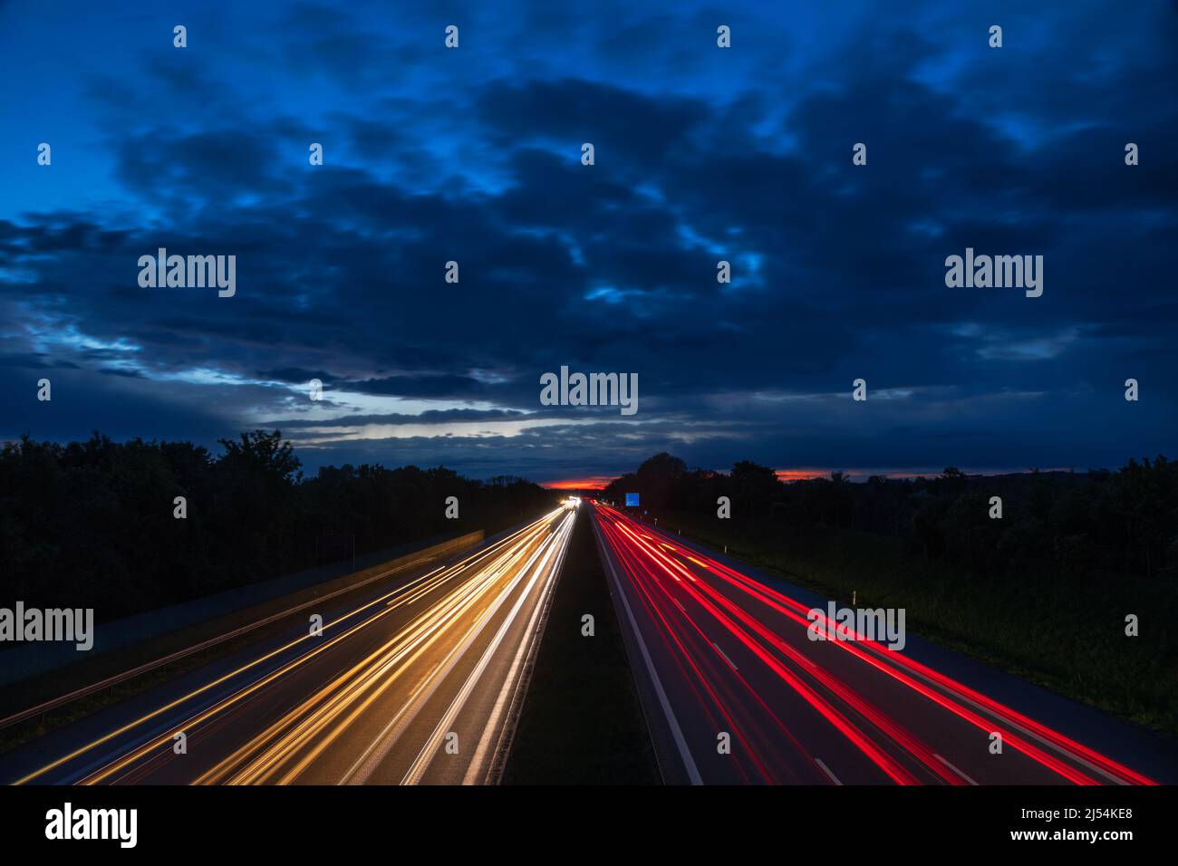 Dramatic evening sky over highway or motorway with car light trails at night, long exposure shot ...