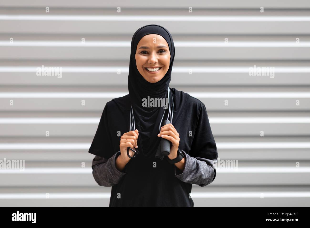 Cheerful pretty millennial muslim female in black hijab with skipping ...