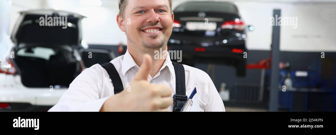 Portrait of a young smiling car mechanic holding thumbs up in car ...
