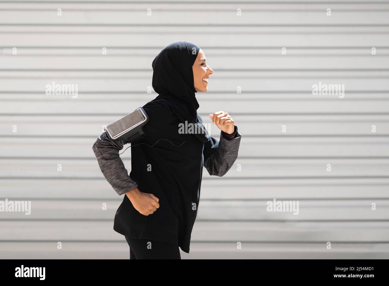 Happy young islamic woman athlete in hijab, sportswear with smartphone ...