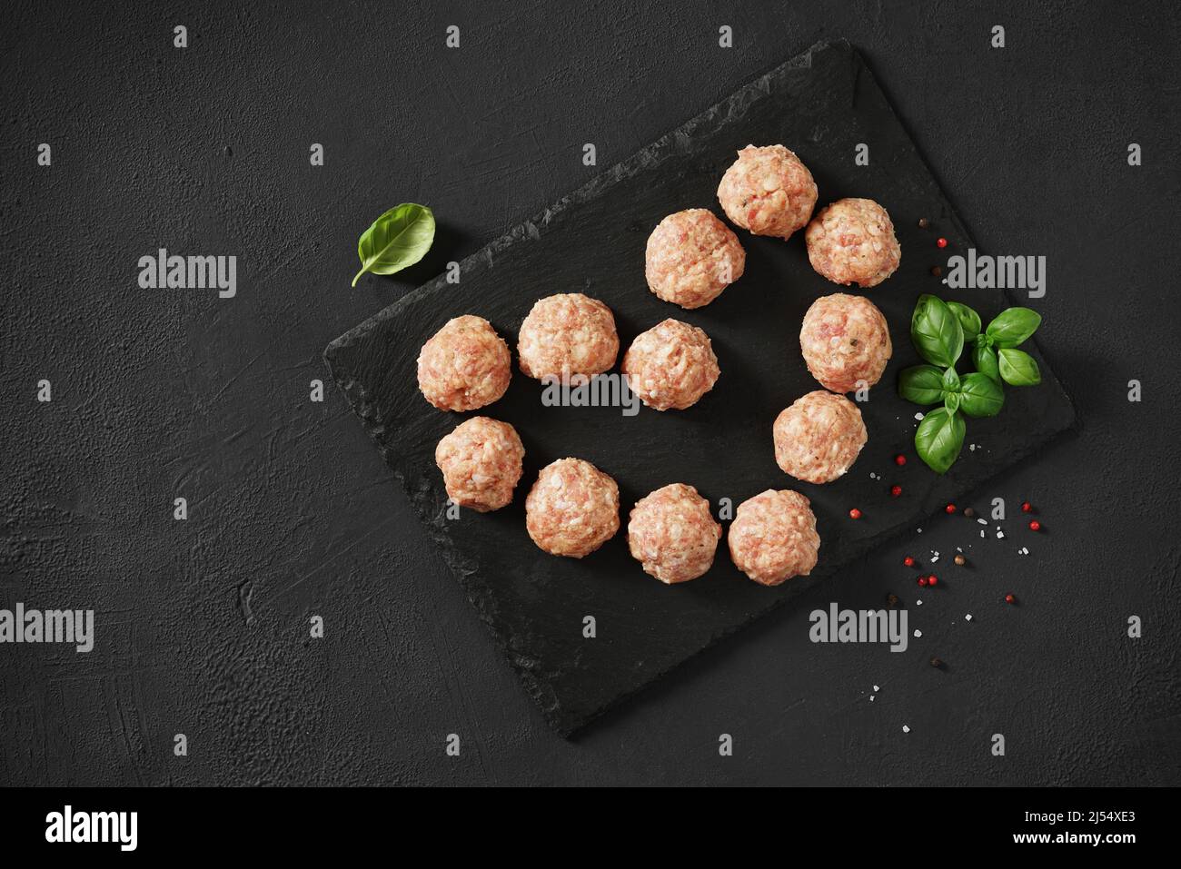 Raw meatballs with basil in heart shape. Black background. Top view ...