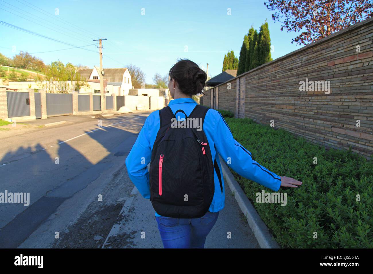 Girl with a backpack is walking along the sidewalk on a sunny day ...