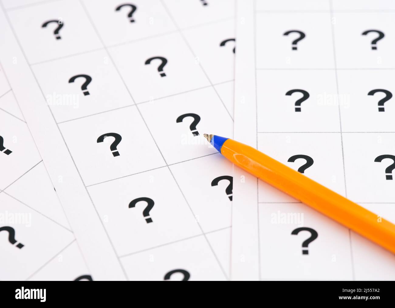 A orange pen laying on pieces of paper that have question marks on them ...