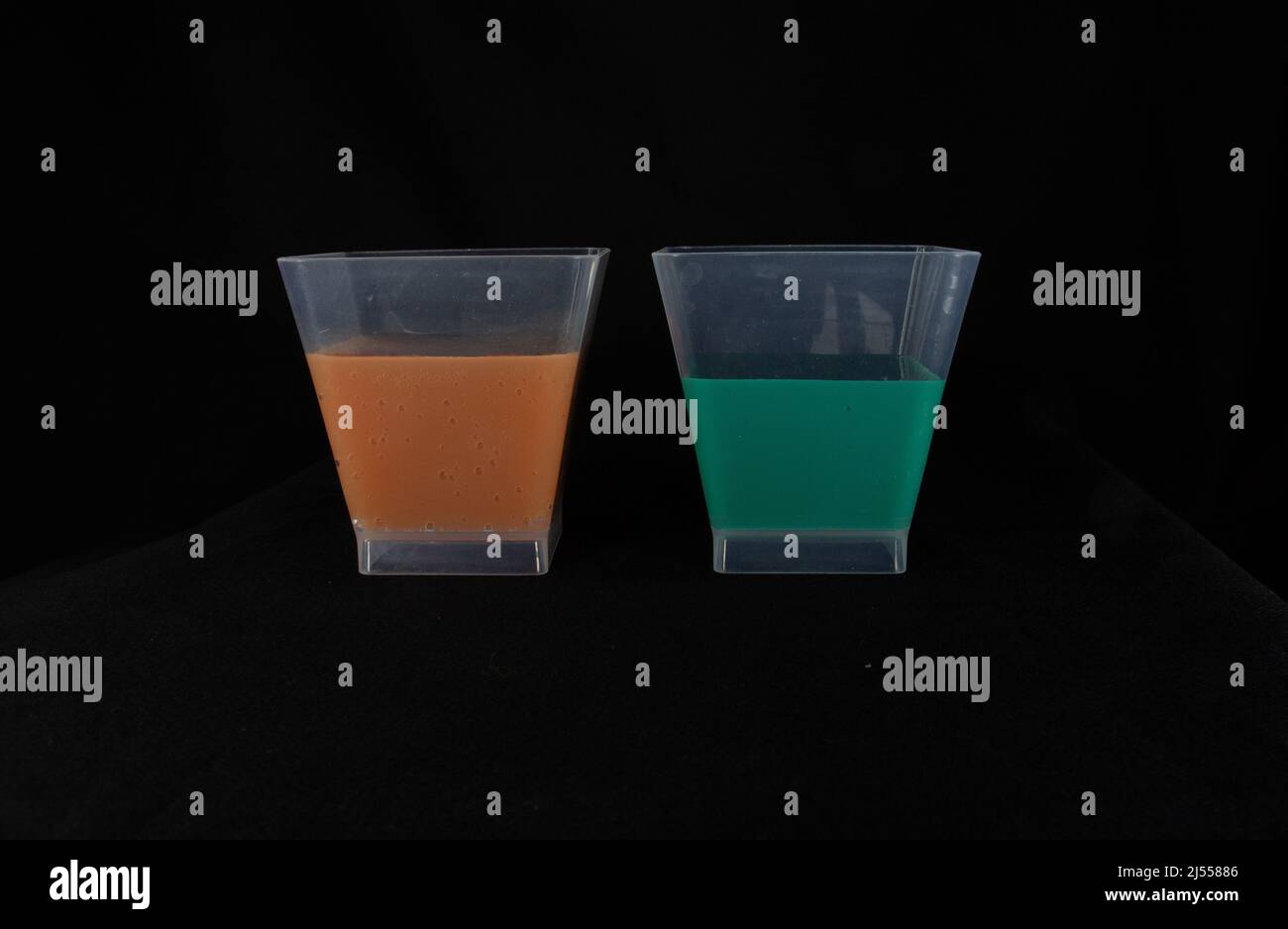 two palstic cups half full of liquid isolated on a black background ...