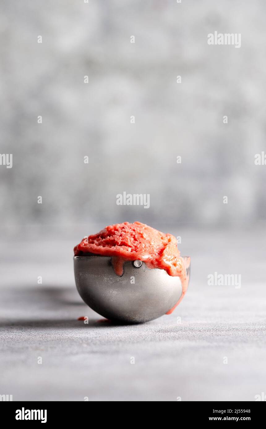 A scoop of strawberry ice cream melting in a metal scoop on a grey ...