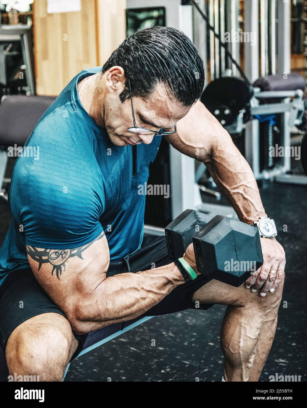 Stock photo of a Muscle man trains biceps with dumbbells at the gym ...