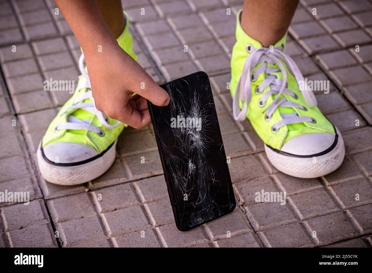 smartphone device with broken screen being picked up from floor by ...