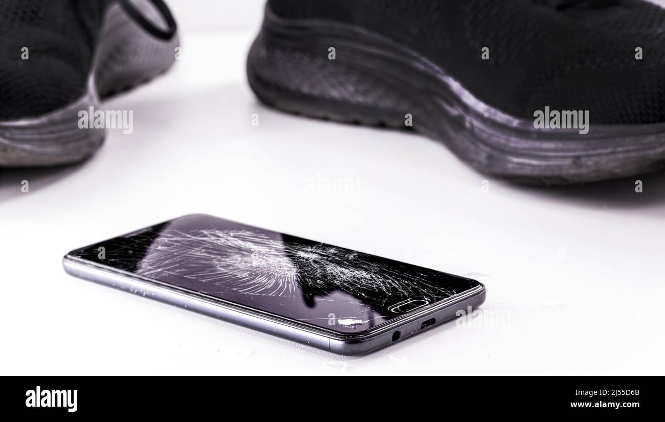 smartphone device fallen on white floor, screen and film cracked in the ...