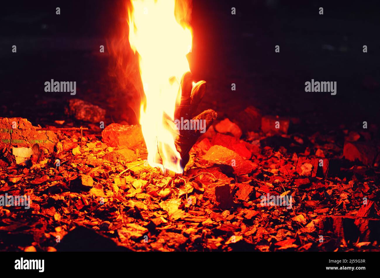 Front view of red flame of raging fire comes from mitten lying on rock ...