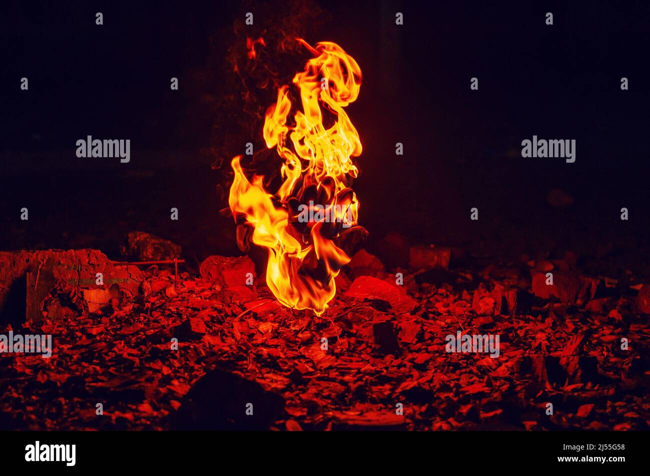 Red flame of burning fire rising from stone covered with autumn leaves ...