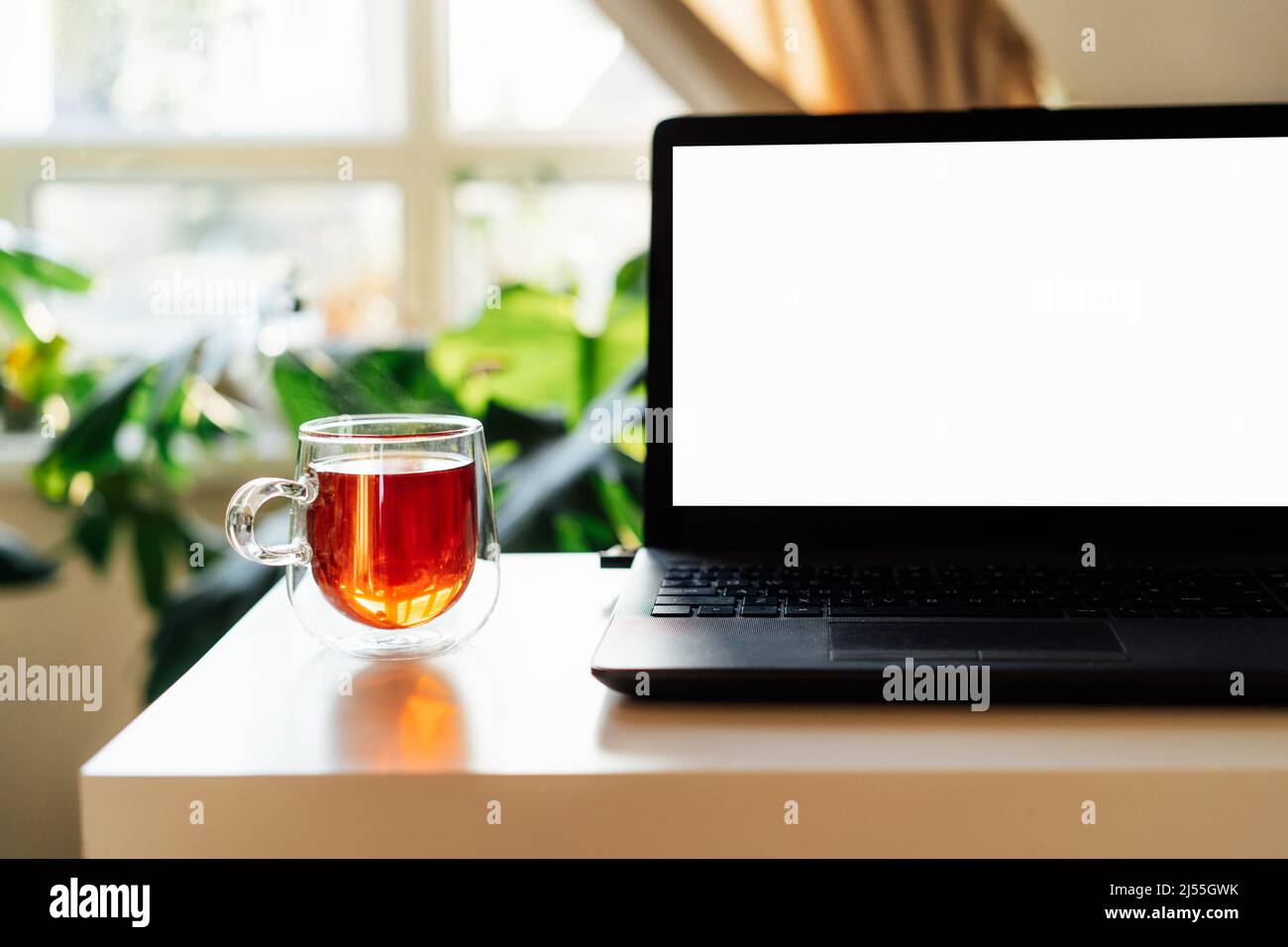 Modern workplace - desk with laptop mockup white screen, cup of tea at ...
