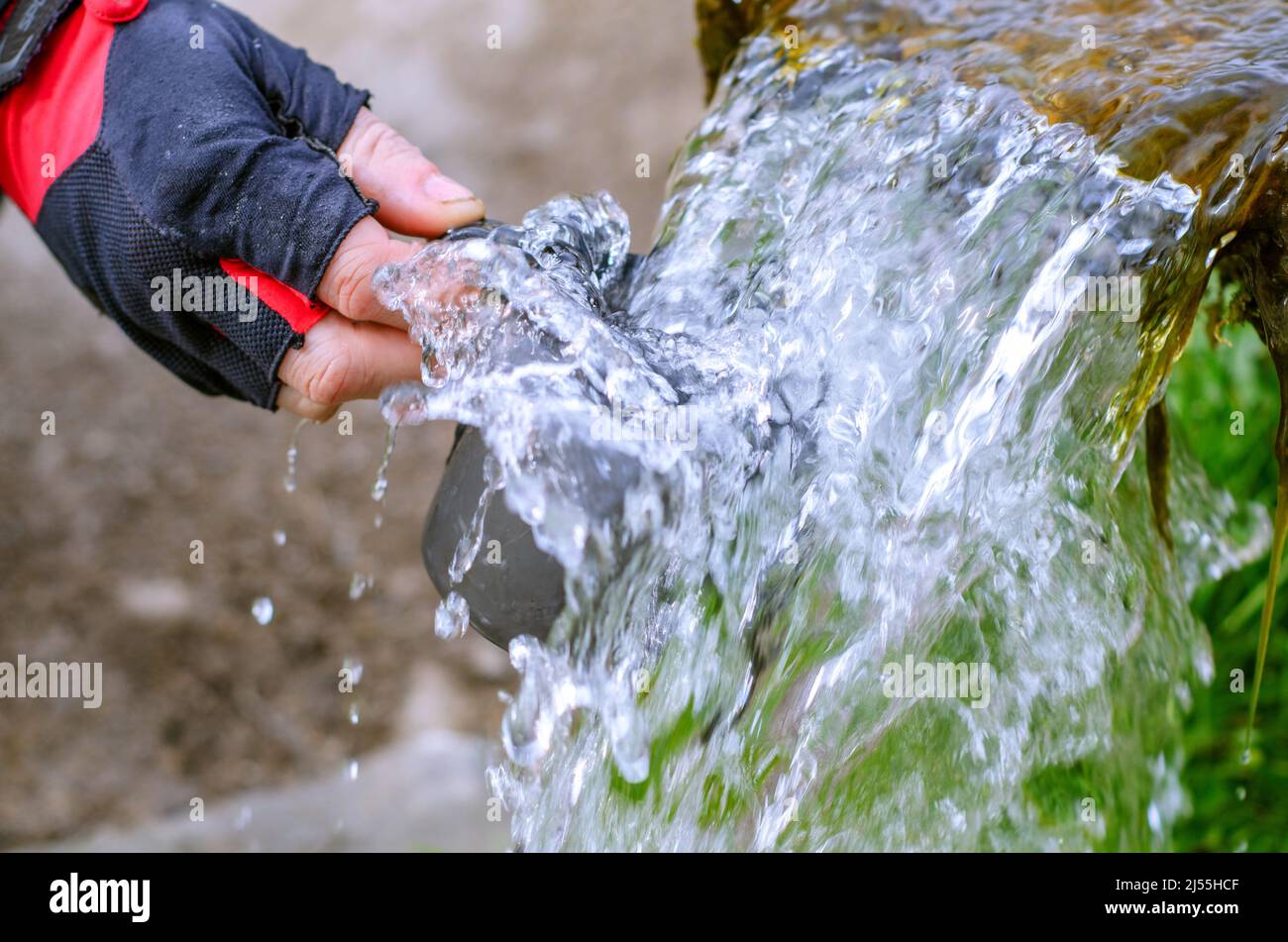 The flow of pure spring water. Man's hand collects water in mug in ...